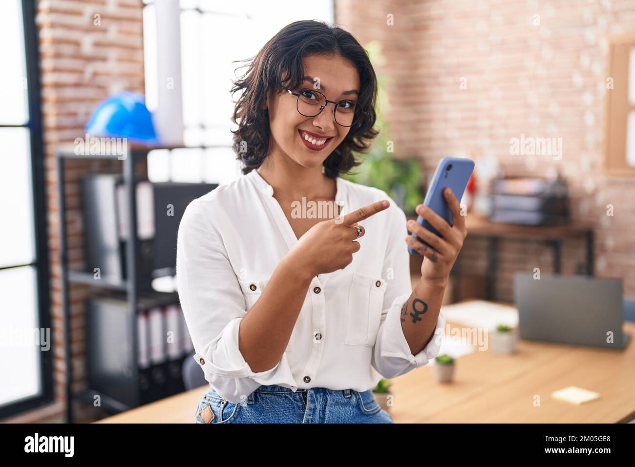 Young hispanic woman working at the office using smartphone smiling ...