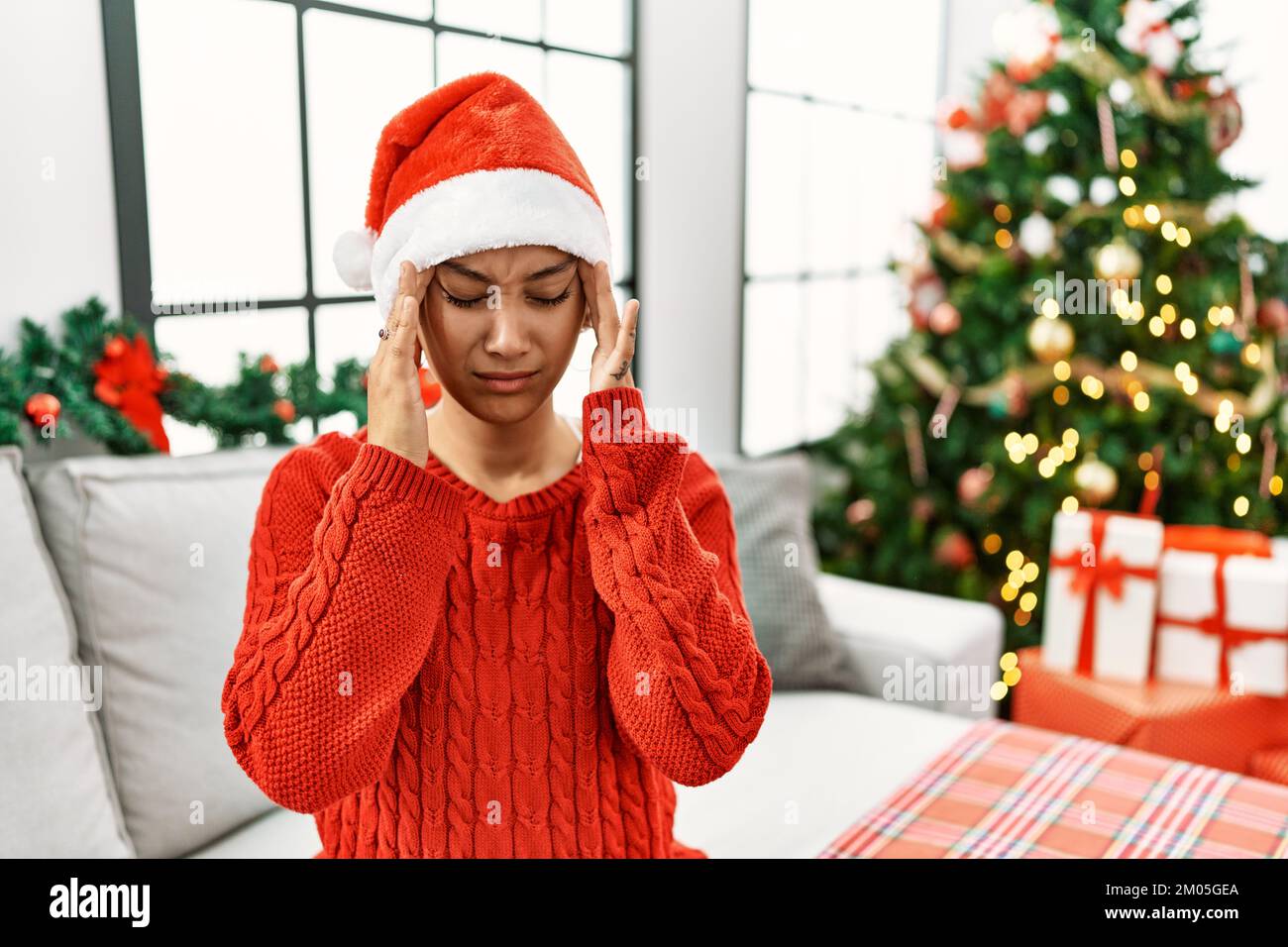 Young hispanic woman with short hair wearing christmas hat sitting on ...