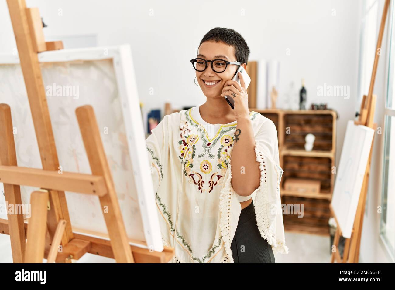 Young hispanic woman talking on the smartphone drawing at art studio ...