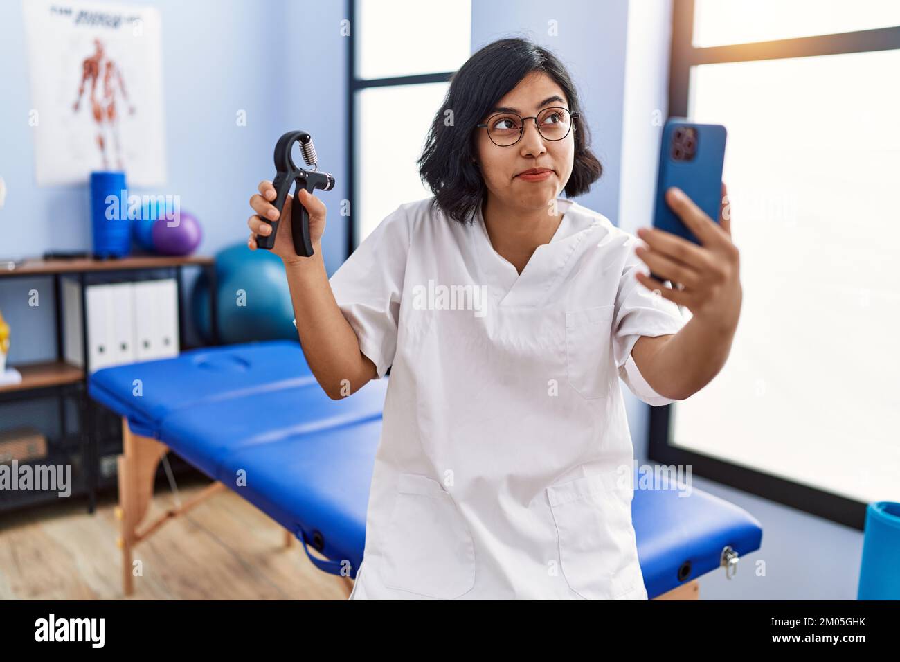 Young hispanic physiotherapist woman holding hand grip to train muscle ...