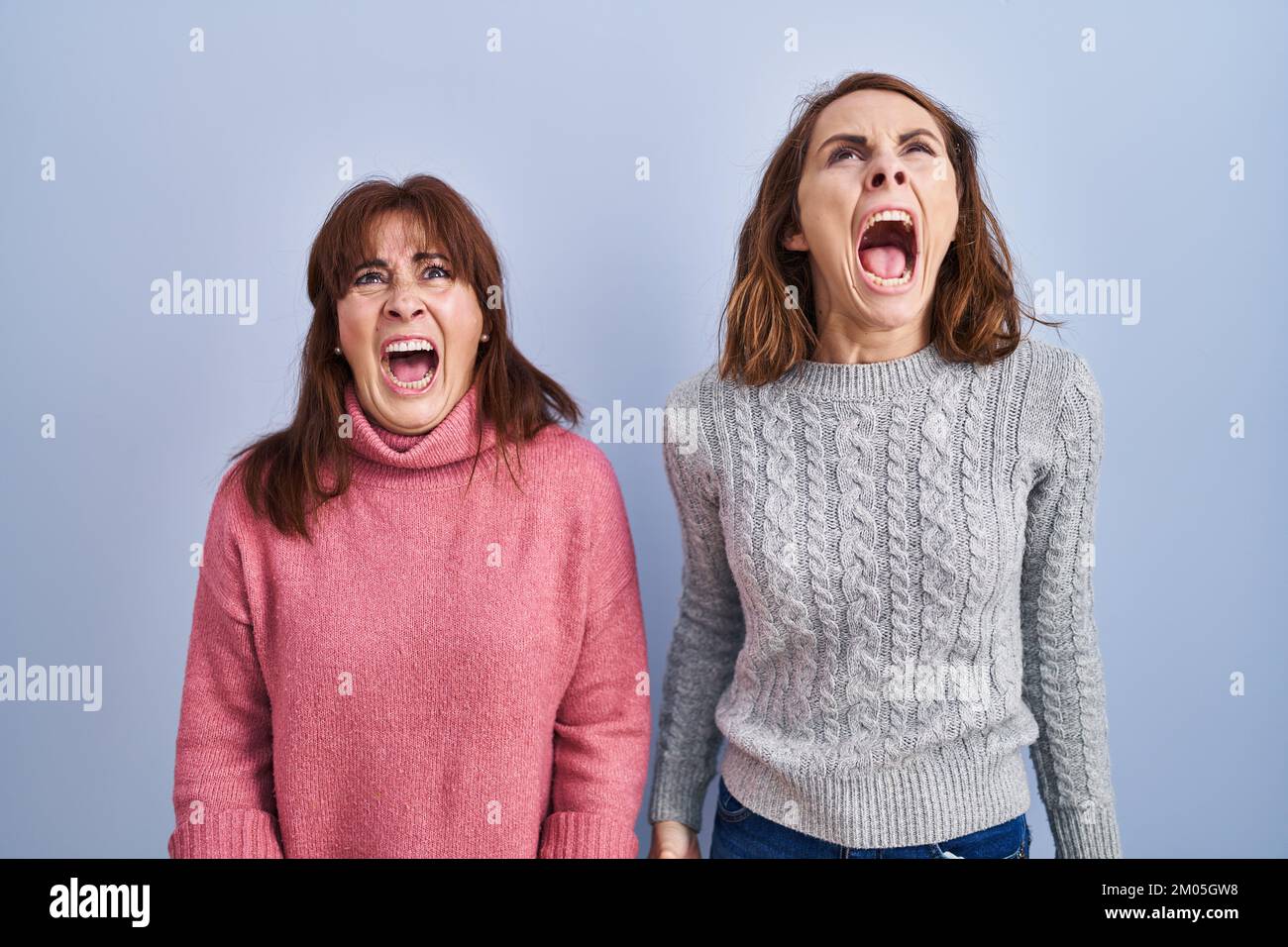 Mother and daughter standing over blue background angry and mad ...