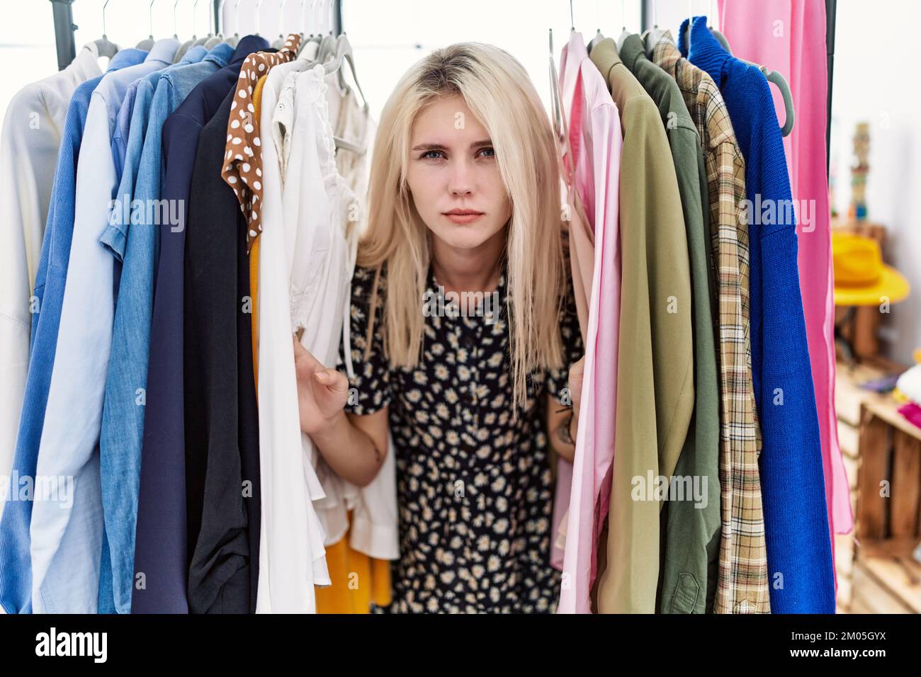 Young blonde woman searching clothes on clothing rack depressed and ...