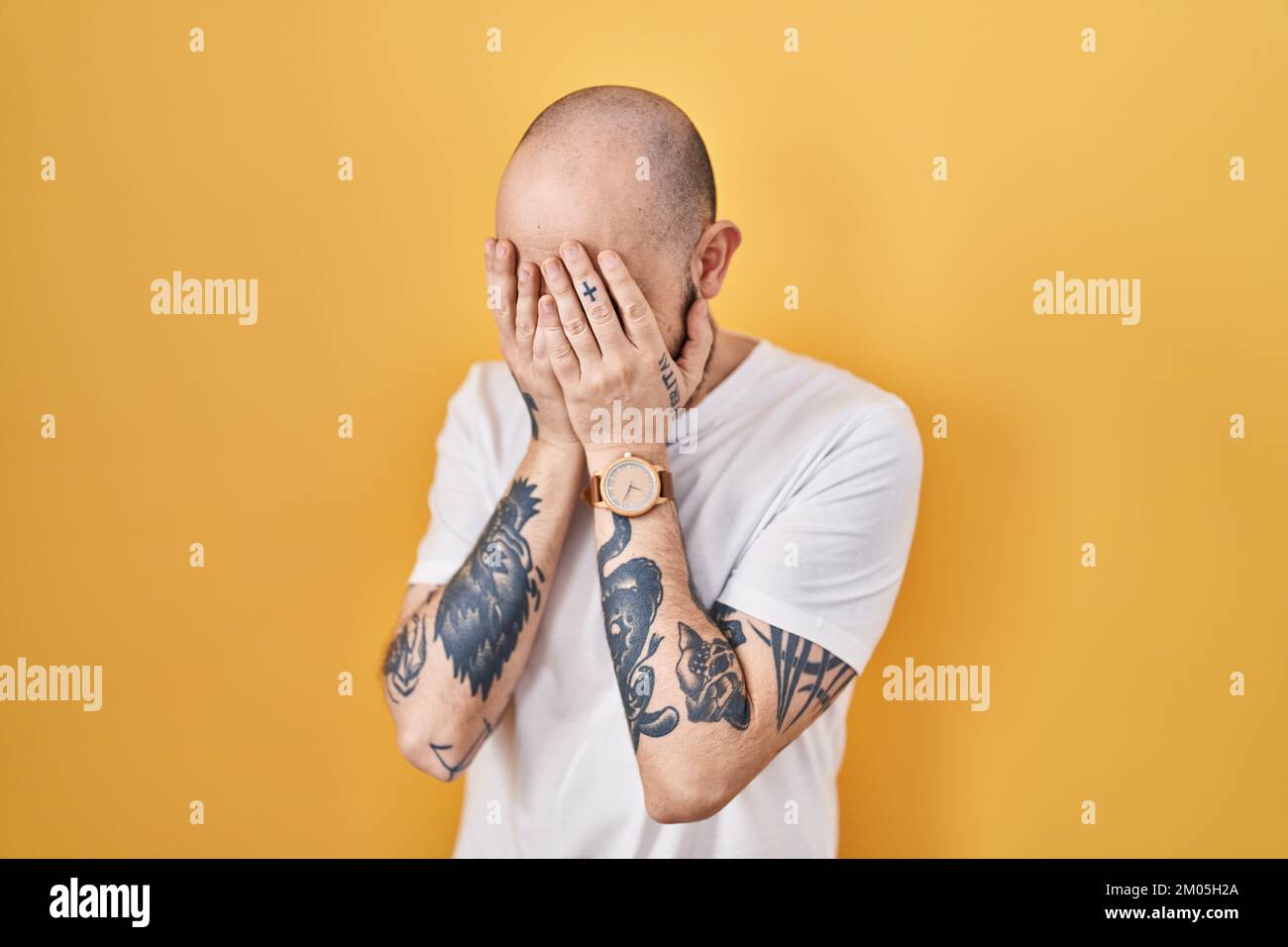 Young hispanic man with tattoos standing over yellow background with ...