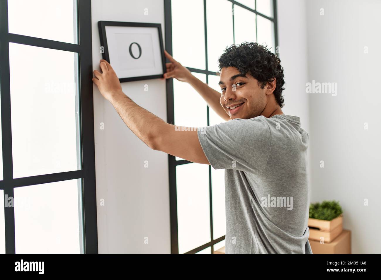 Young hispanic man smiling happy hanging frame at new home Stock Photo ...