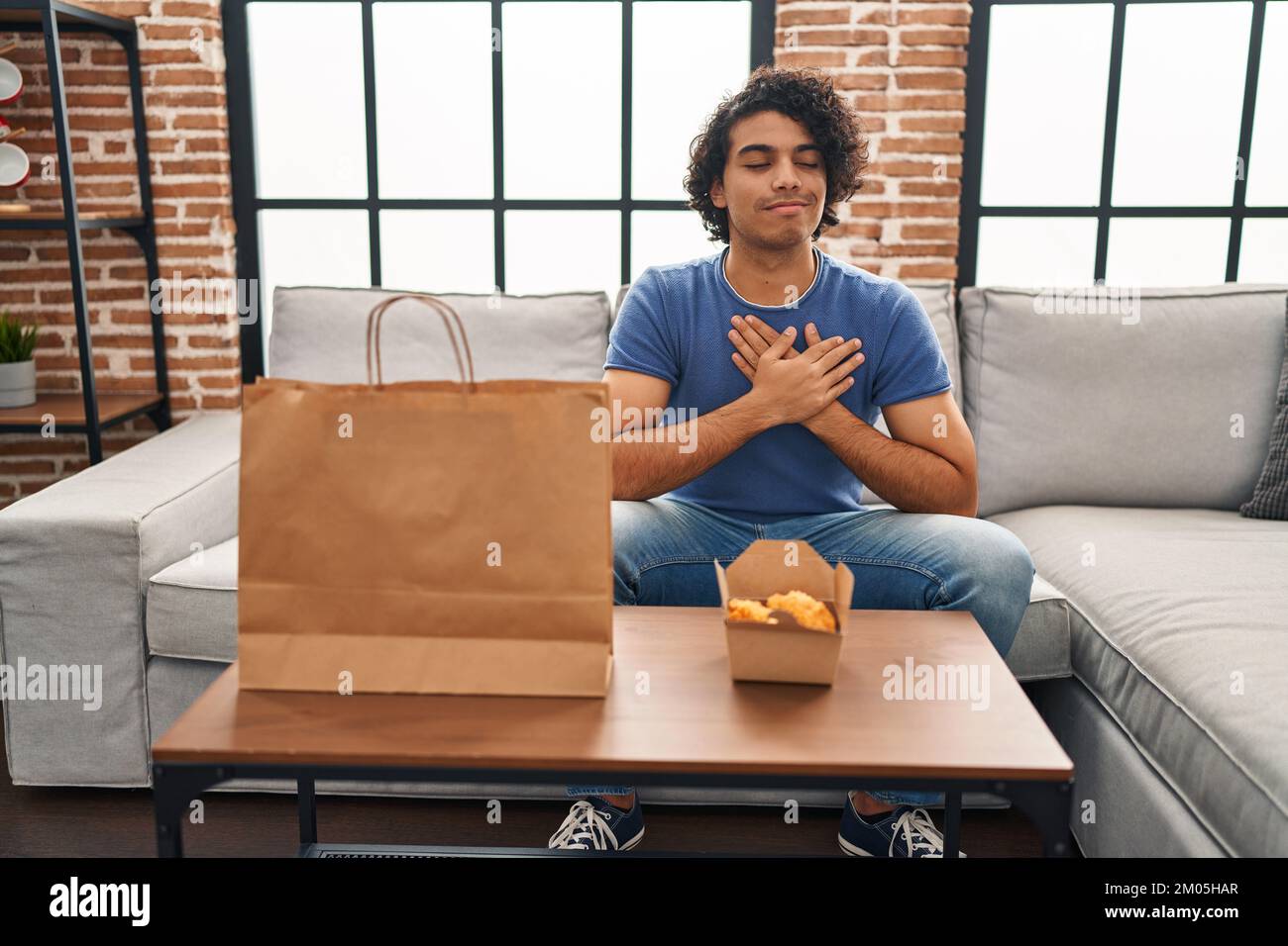 Hispanic man with curly hair eating chicken wings smiling with hands on ...
