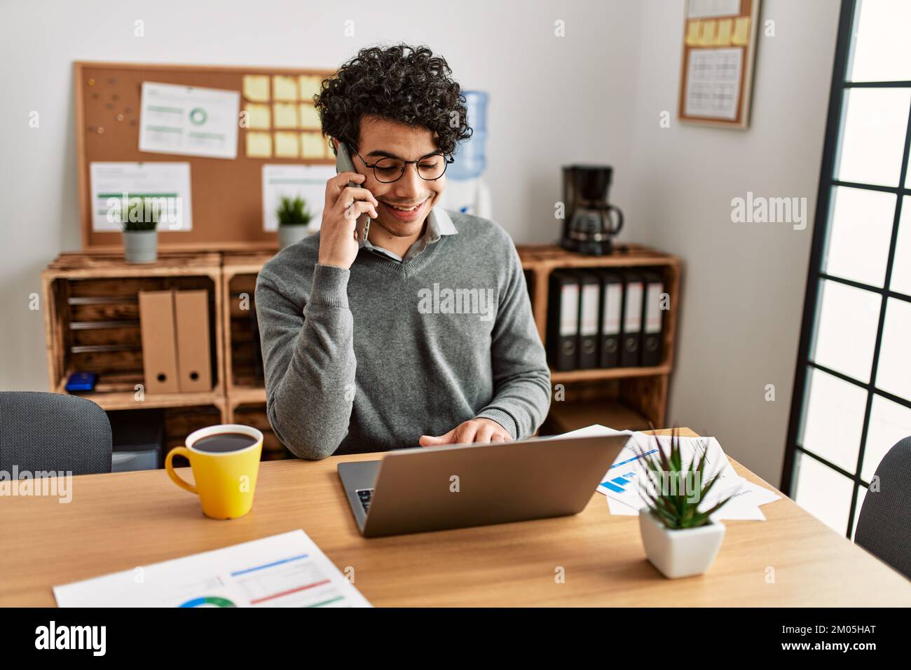 Young hispanic businessman talking on the smartphone and using laptop ...