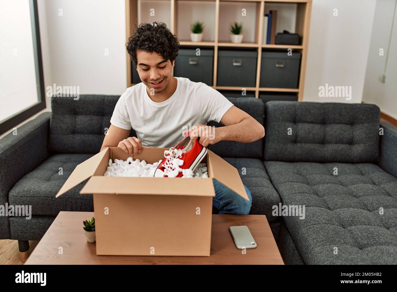 Young hispanic man unboxing sneakers of cardboard box sitting on the ...