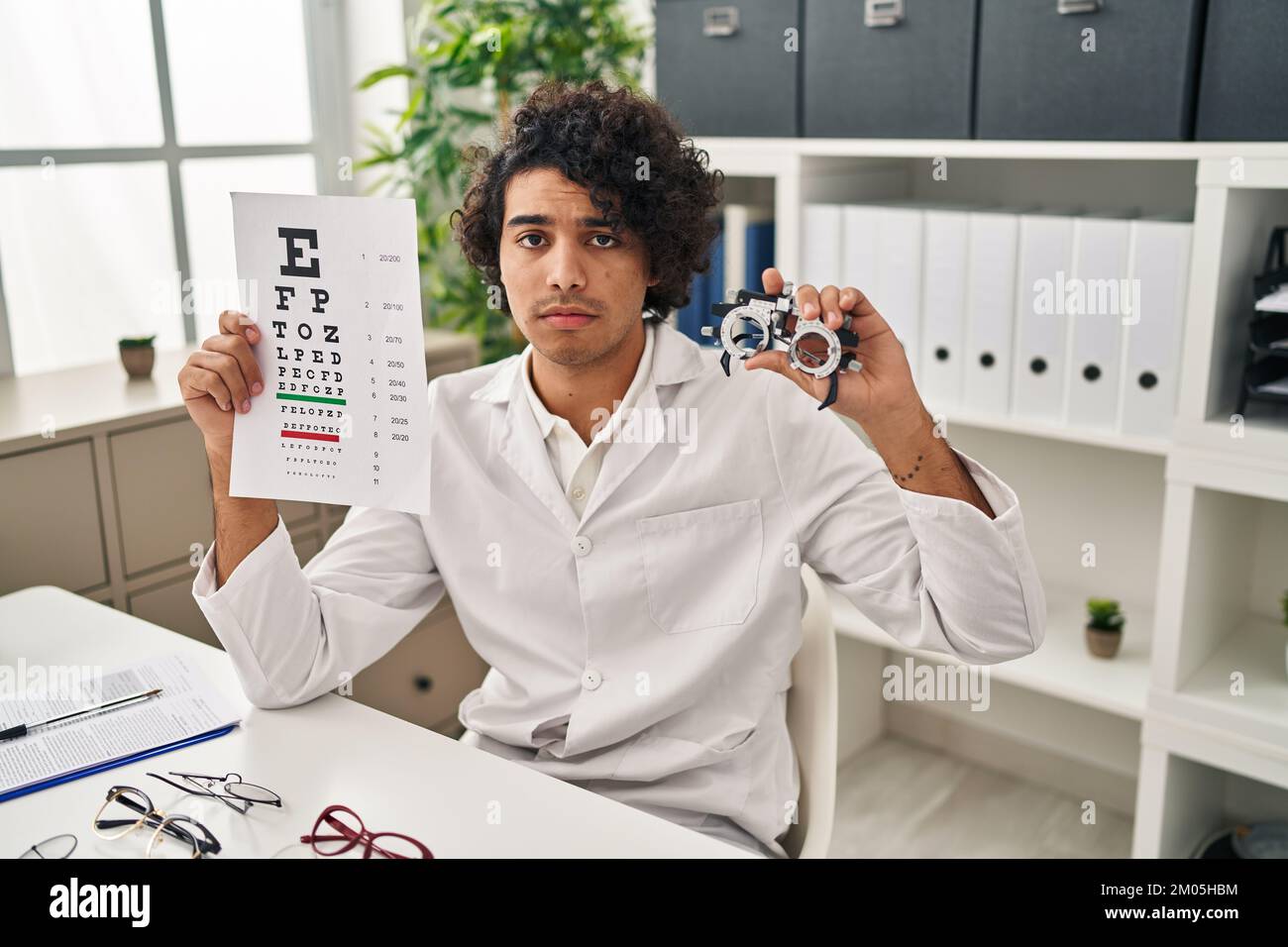 Hispanic man with curly hair holding optometry glasses and eyesight ...