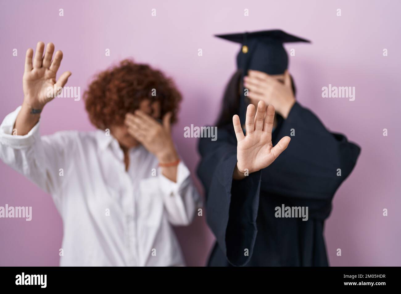 Hispanic mother and daughter wearing graduation cap and ceremony robe ...