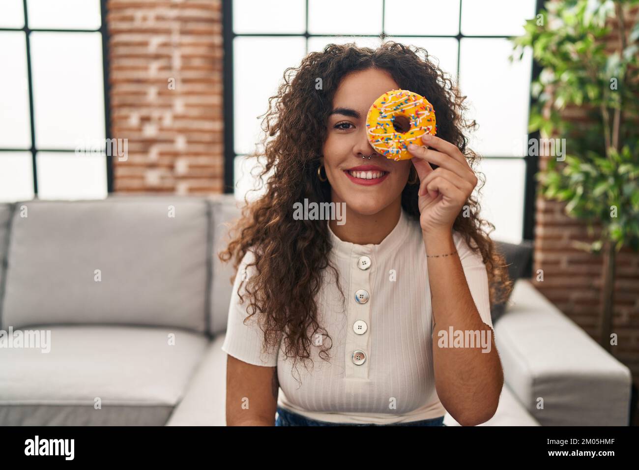 Young hispanic woman holding tasty colorful doughnut eye looking ...