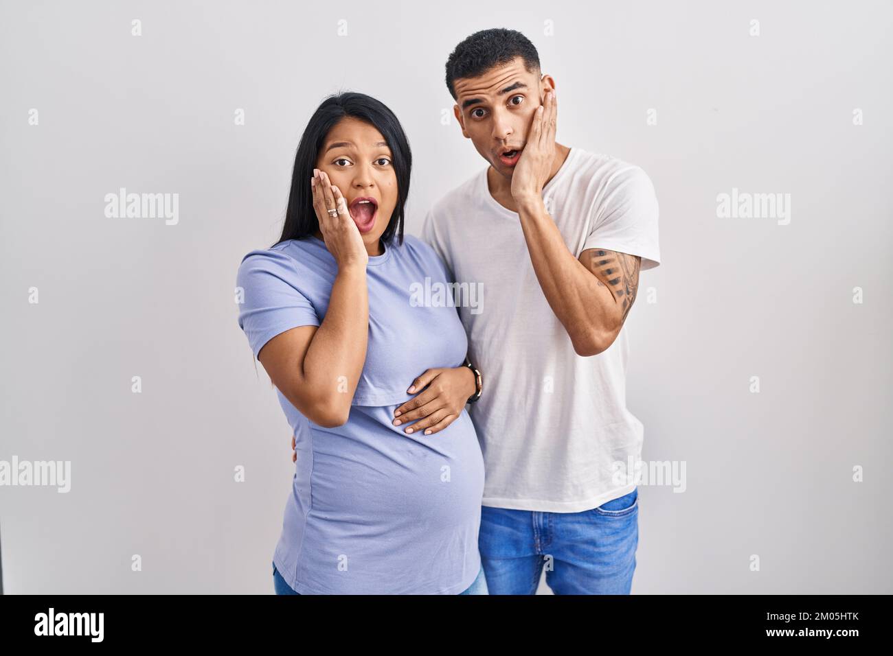 Young hispanic couple expecting a baby standing over background afraid ...