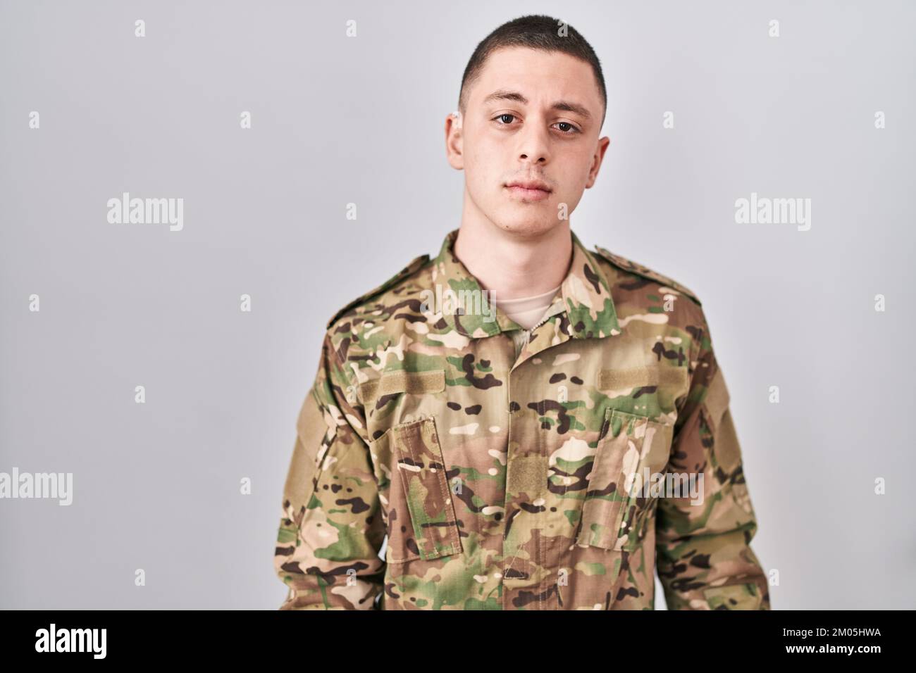 Young man wearing camouflage army uniform relaxed with serious ...