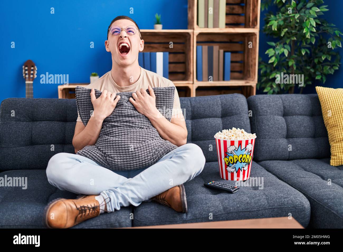 Young man eating popcorn angry and mad screaming frustrated and furious ...