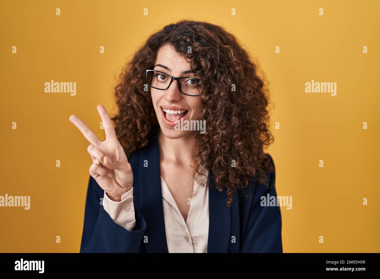 Hispanic woman with curly hair standing over yellow background smiling ...