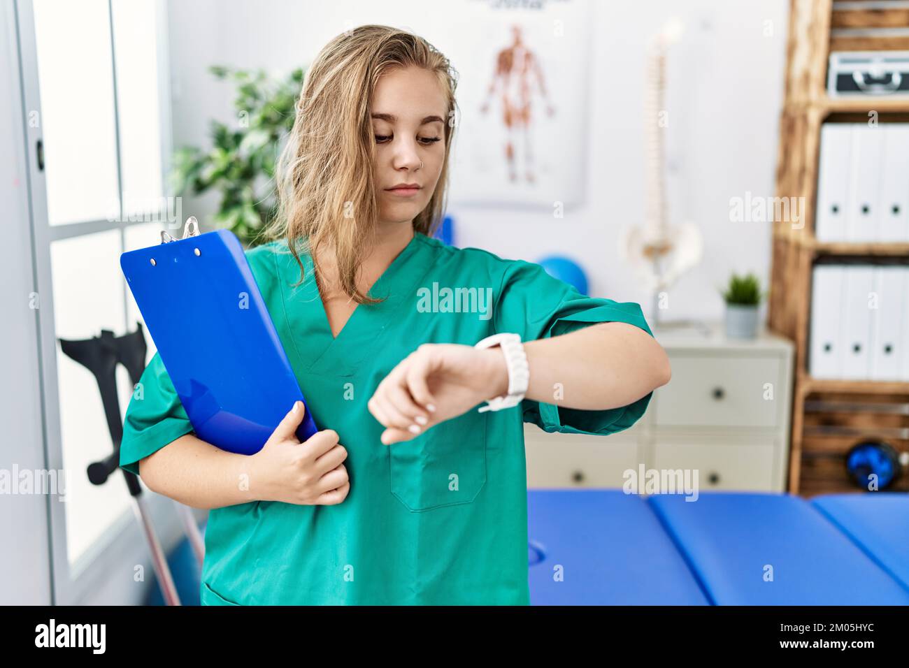 Young caucasian woman working at pain recovery clinic checking the time ...
