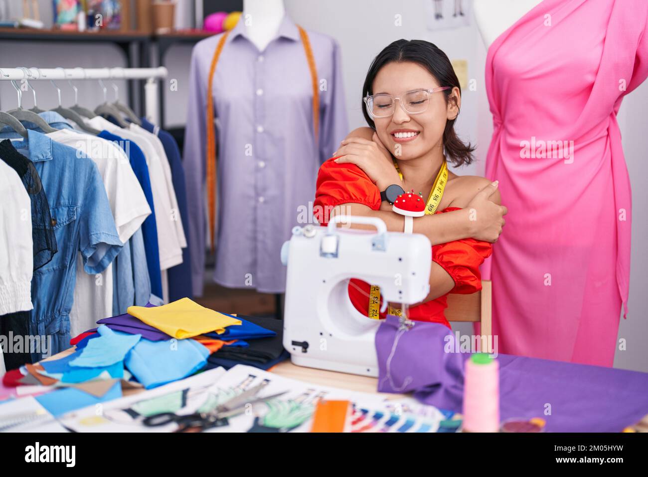 Hispanic young woman dressmaker designer using sewing machine hugging ...