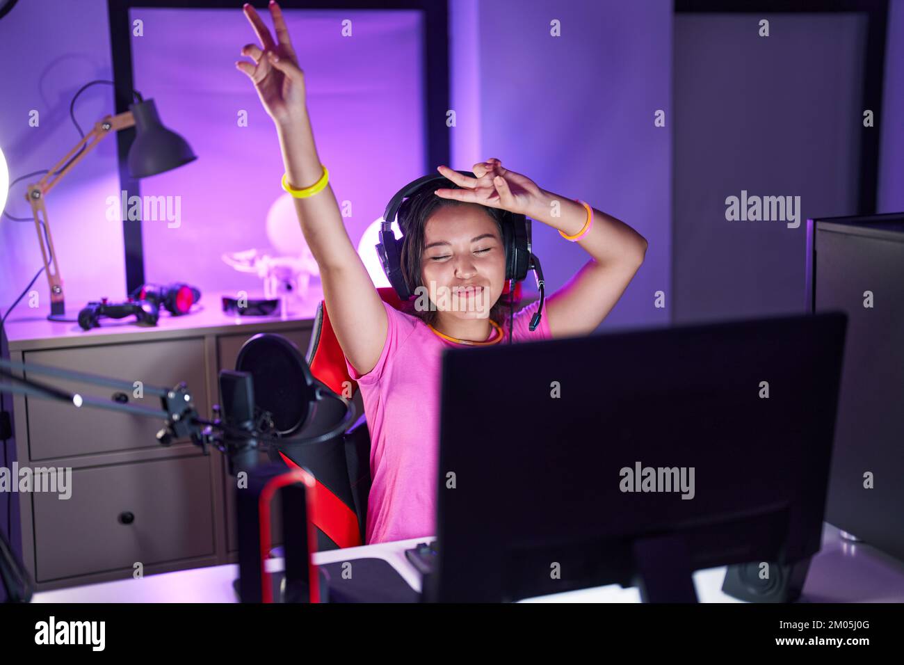 Young hispanic woman streamer playing video game dancing at gaming room ...