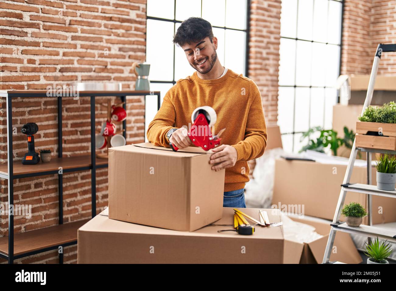 Young hispanic man smiling confident packing cardboard box at new home ...