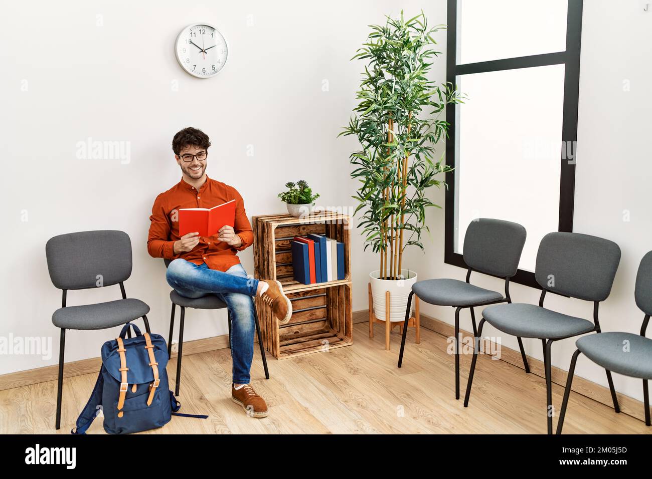 Young hispanic man smiling confident reading book at waiting room Stock ...