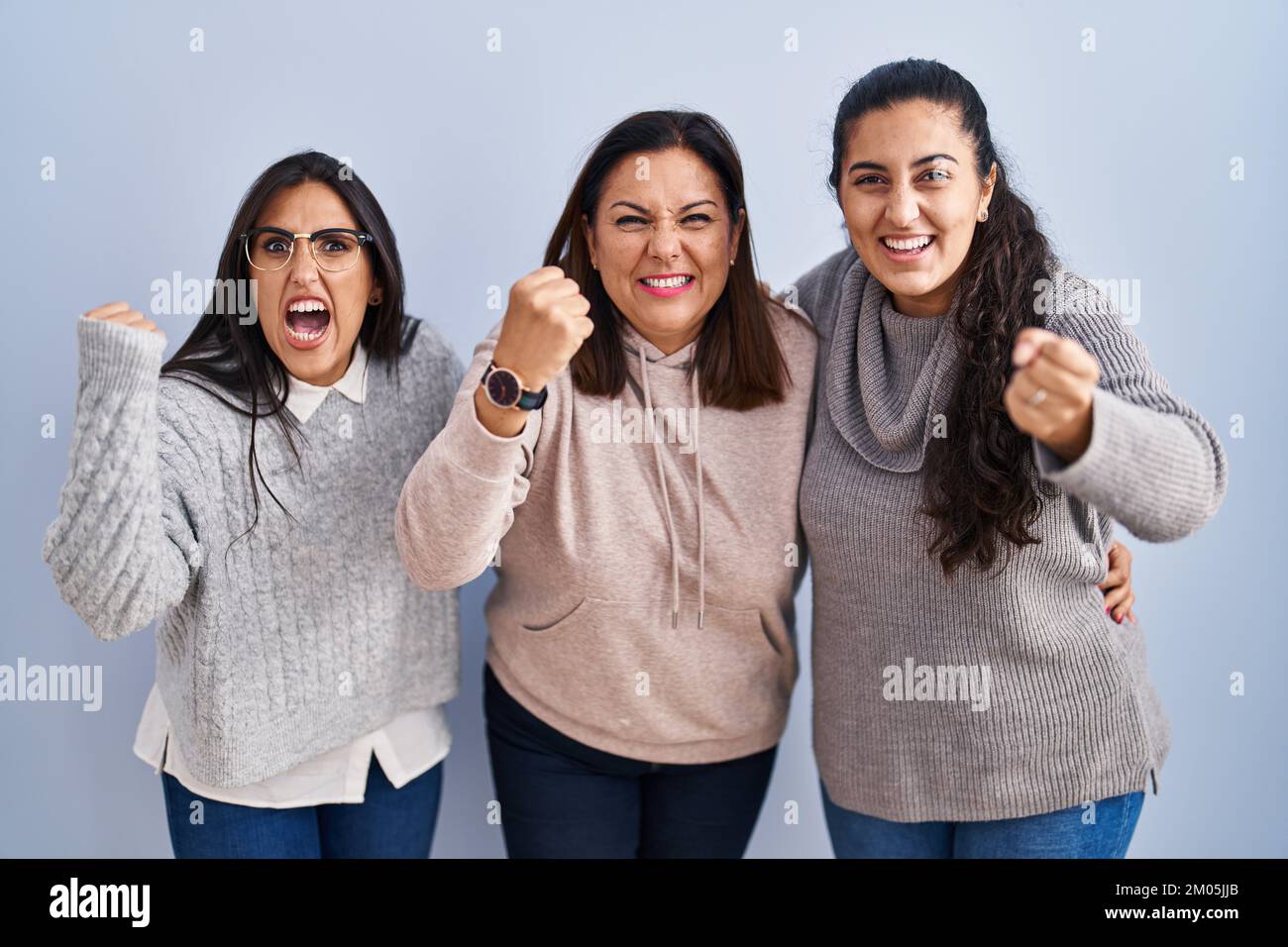 Mother and two daughters standing over blue background angry and mad ...