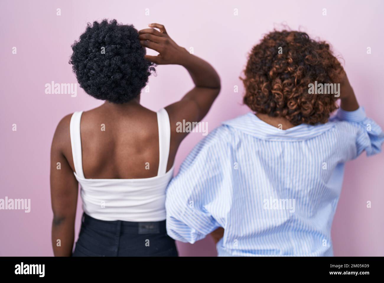 Two african women standing over pink background backwards thinking ...