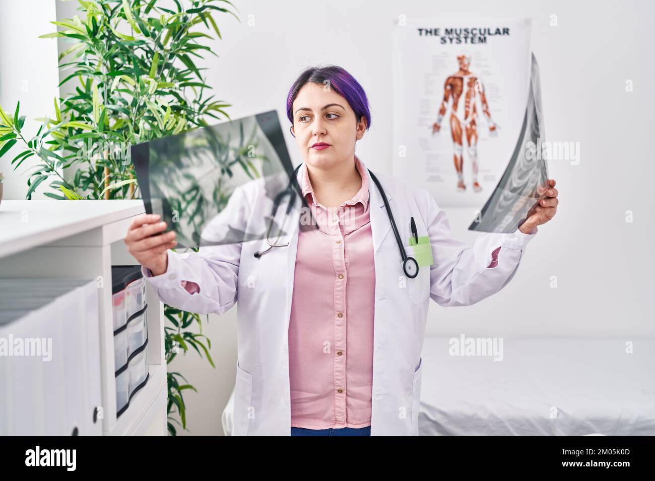 Young beautiful plus size woman doctor looking xray standing at clinic ...