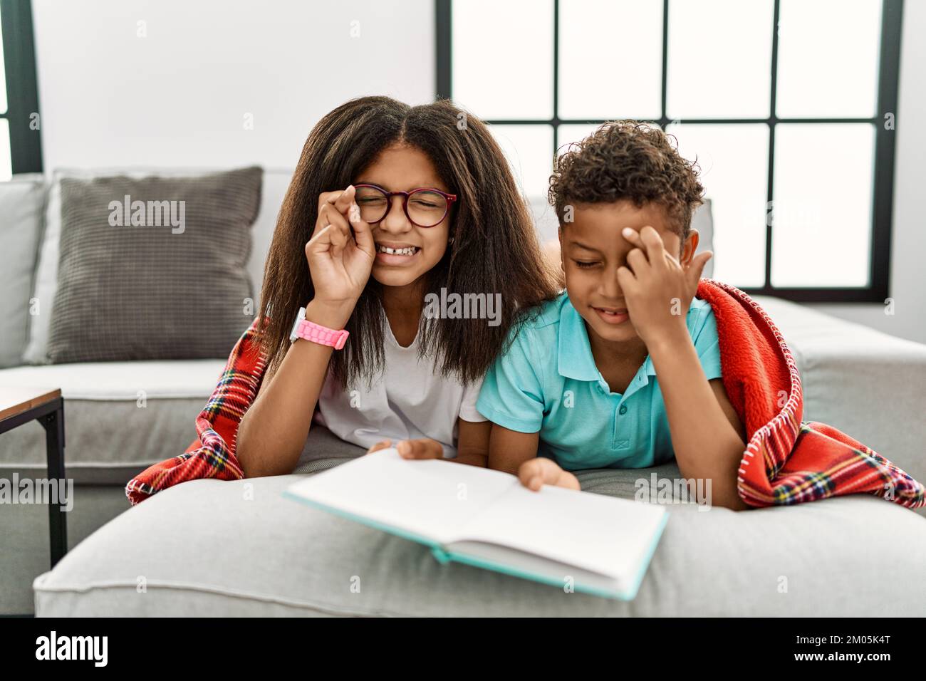 Two siblings lying on the sofa reading a book gesturing finger crossed ...