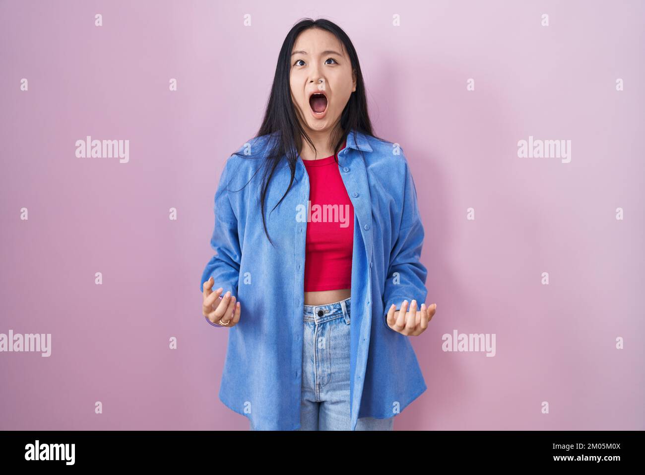 Young asian woman standing over pink background angry and mad screaming ...