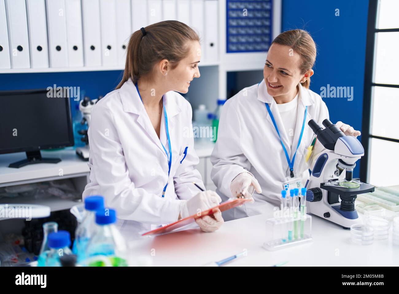 Two women scientists using microscope and write on document at ...