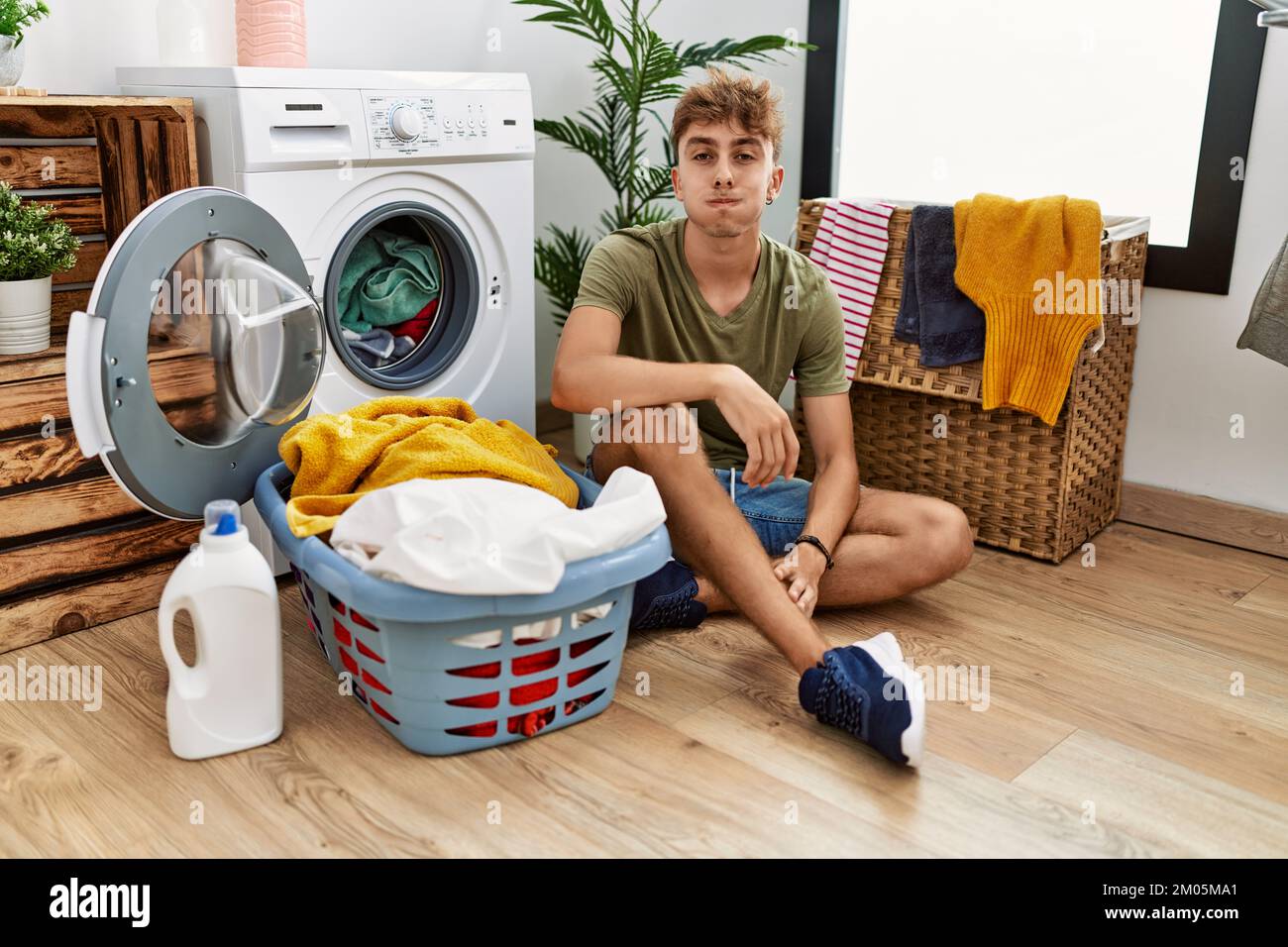 Young caucasian man putting dirty laundry into washing machine puffing ...