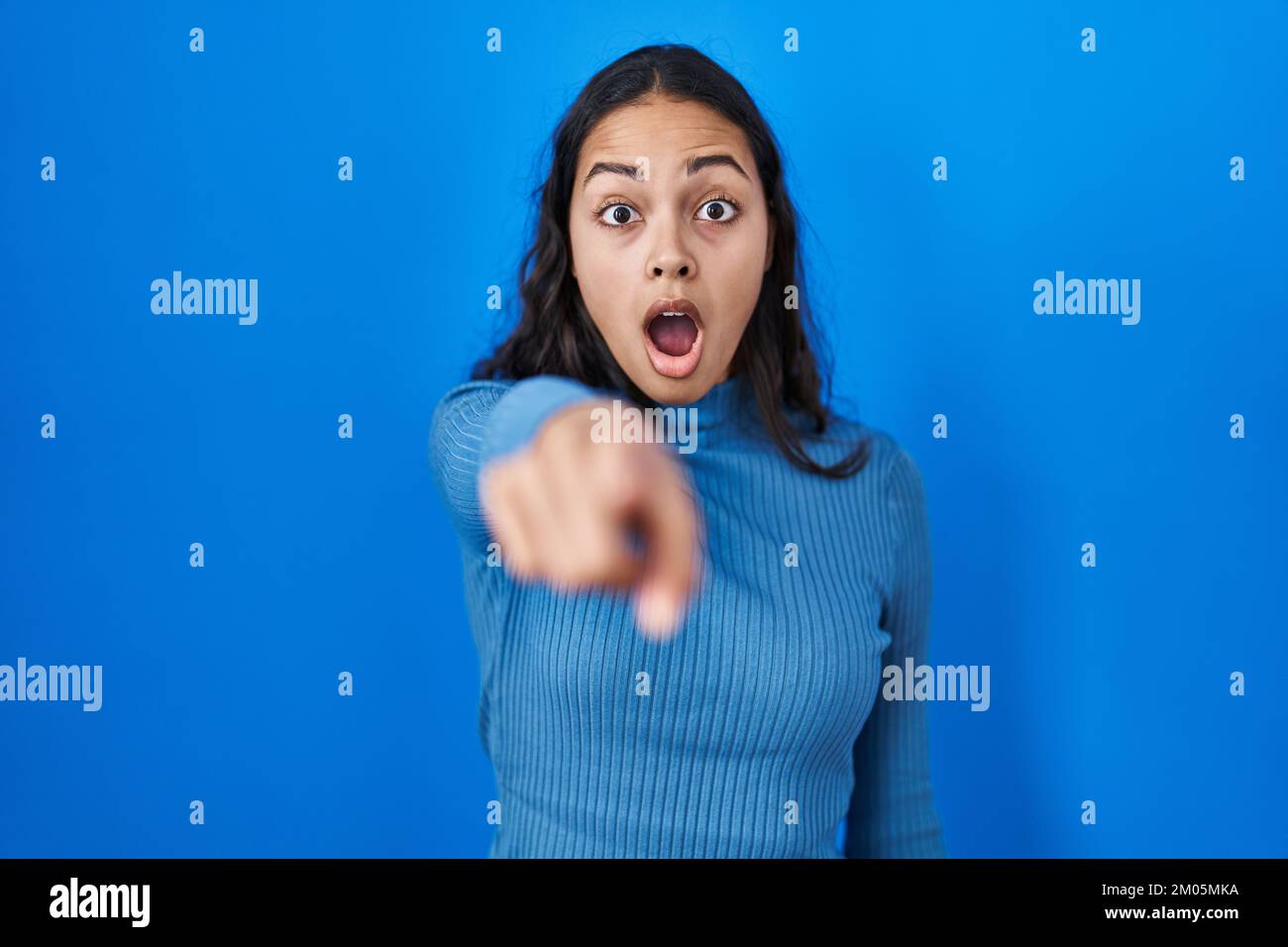 Young brazilian woman standing over blue isolated background pointing ...