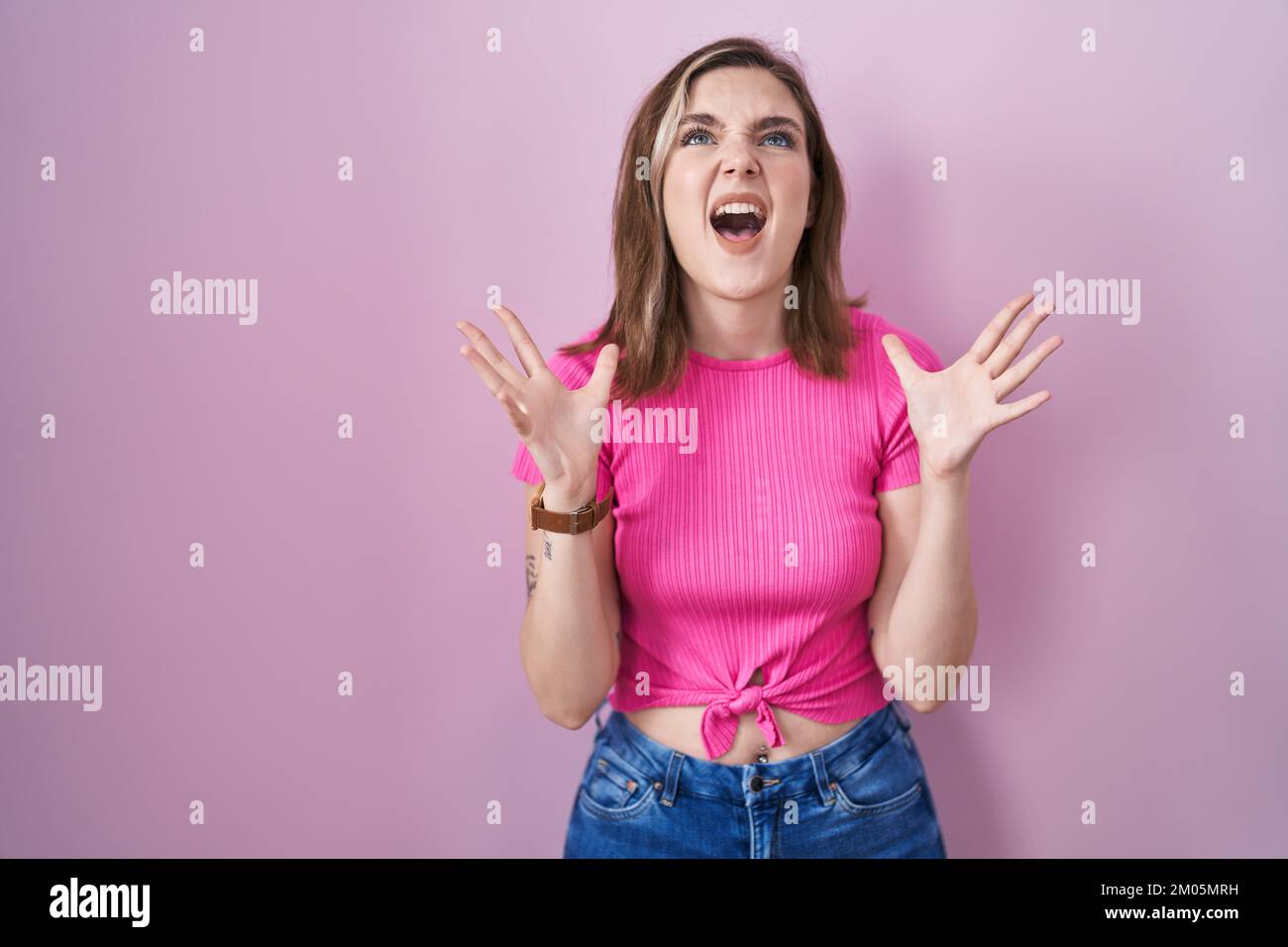 Blonde caucasian woman standing over pink background crazy and mad ...