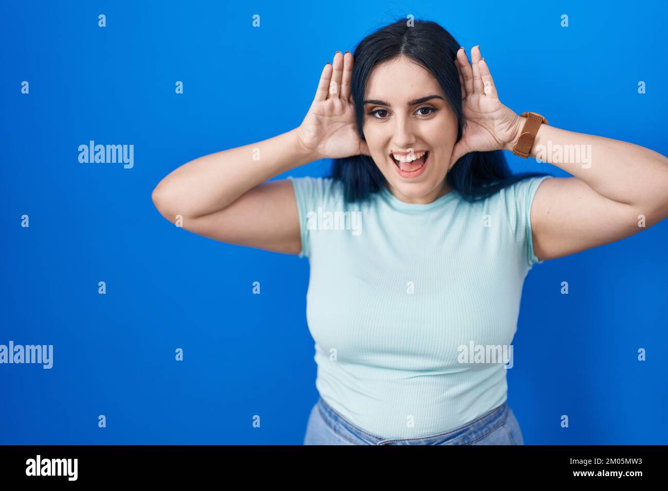 Young modern girl with blue hair standing over blue background smiling ...