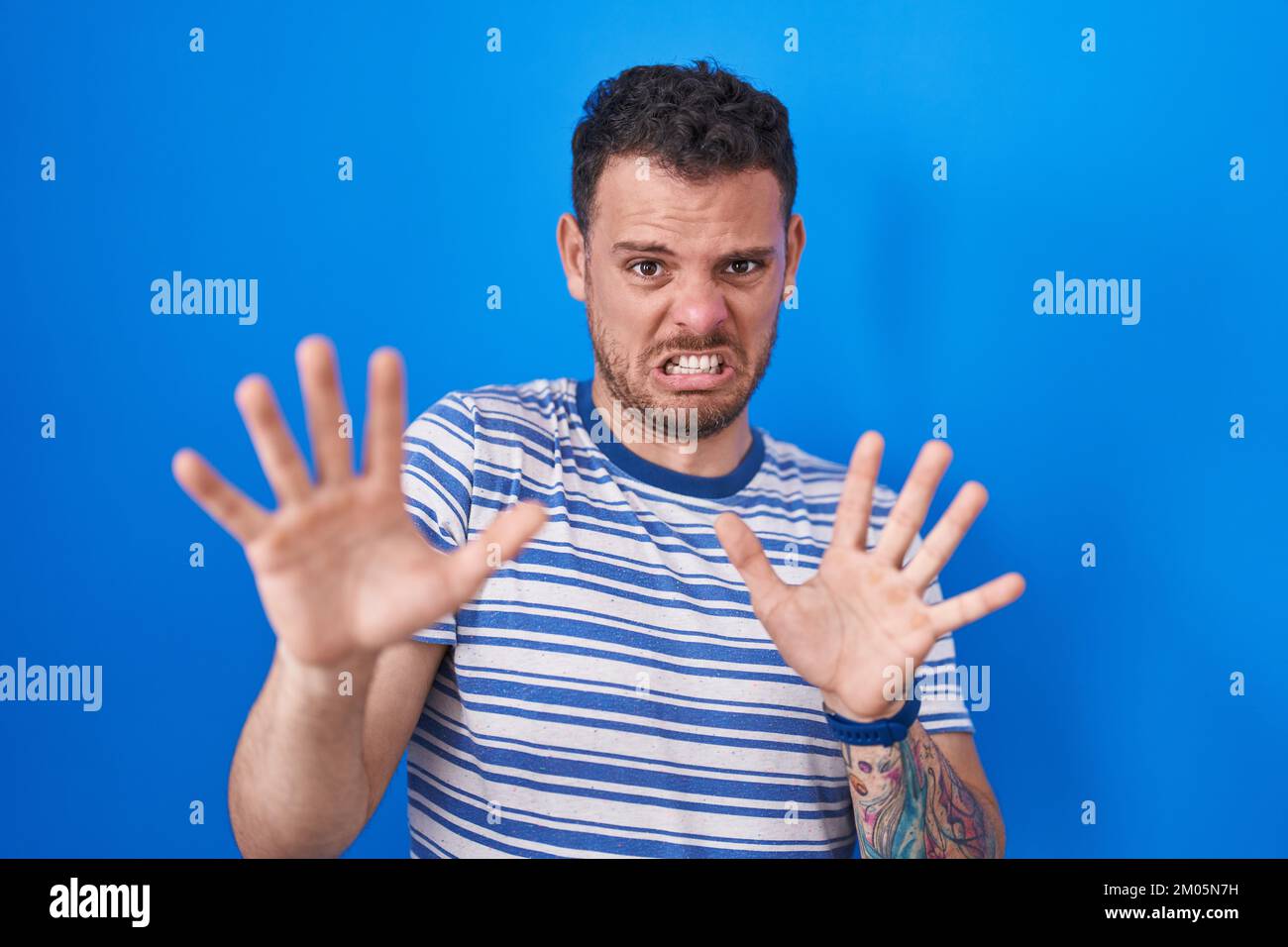 Young hispanic man standing over blue background afraid and terrified ...