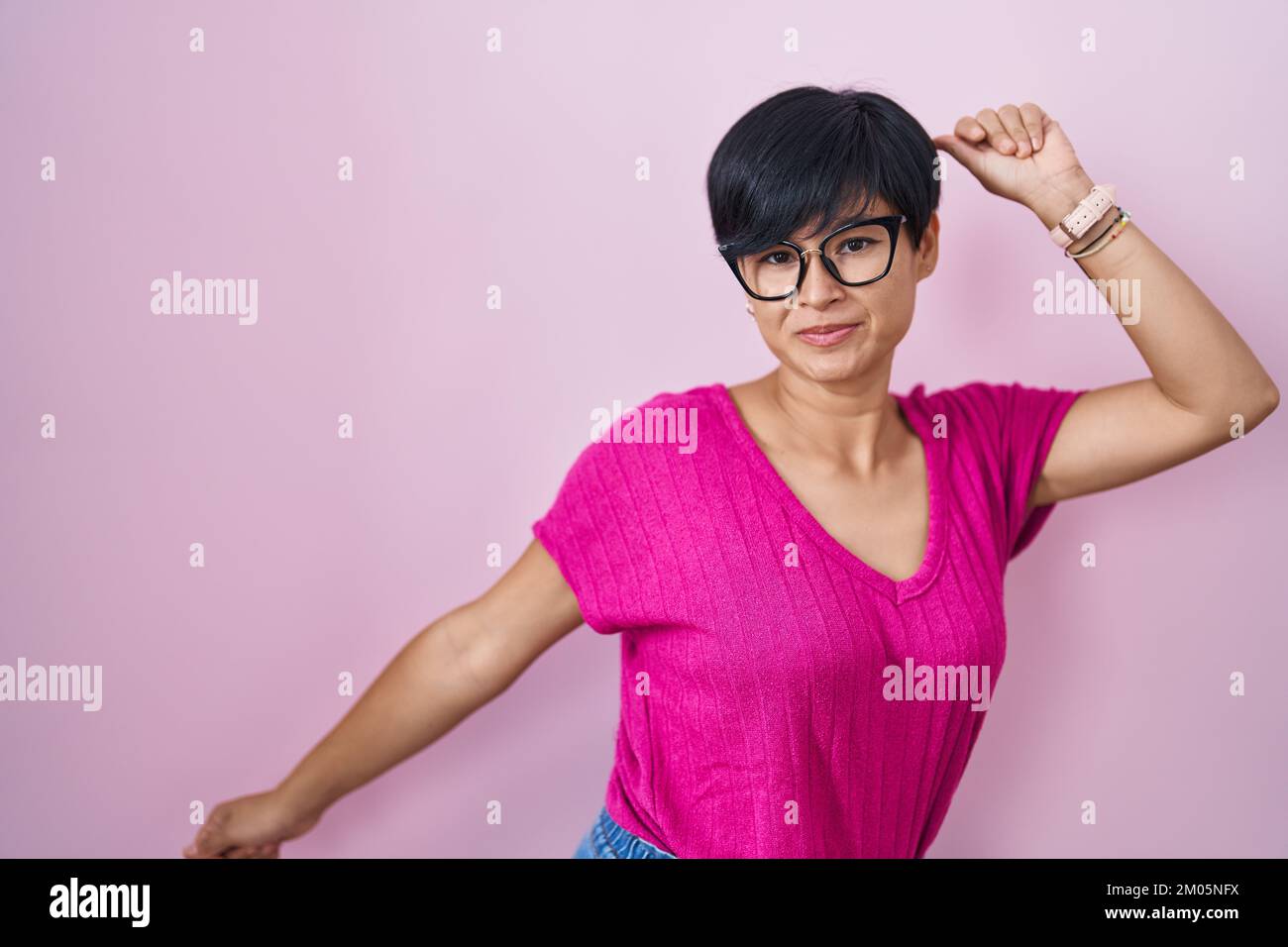 Young asian woman with short hair standing over pink background dancing ...