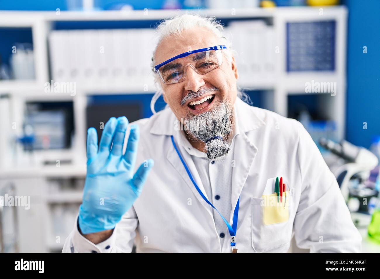 Middle age man with grey hair working at scientist laboratory looking positive and happy ...