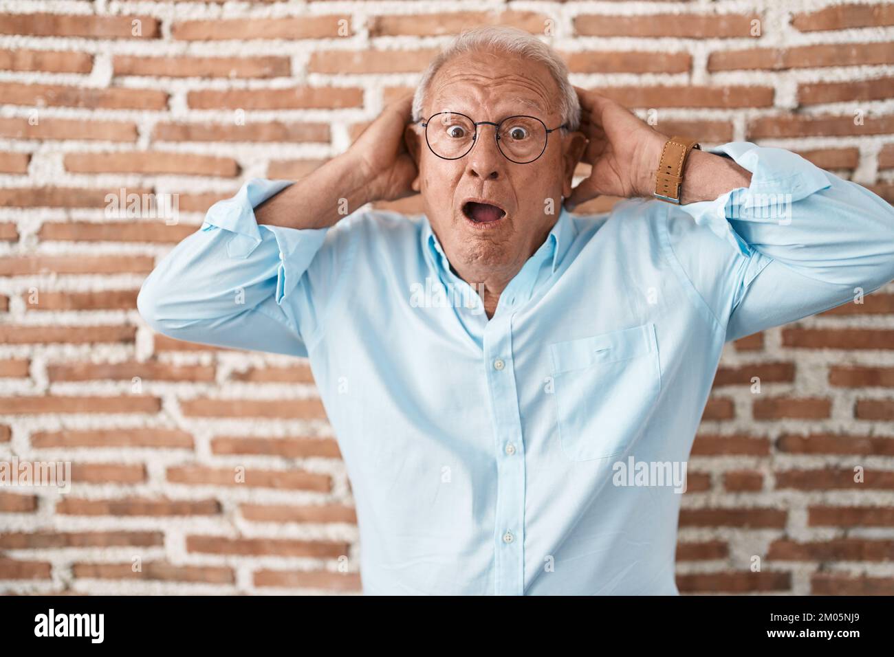 Senior man with grey hair standing over bricks wall crazy and scared ...