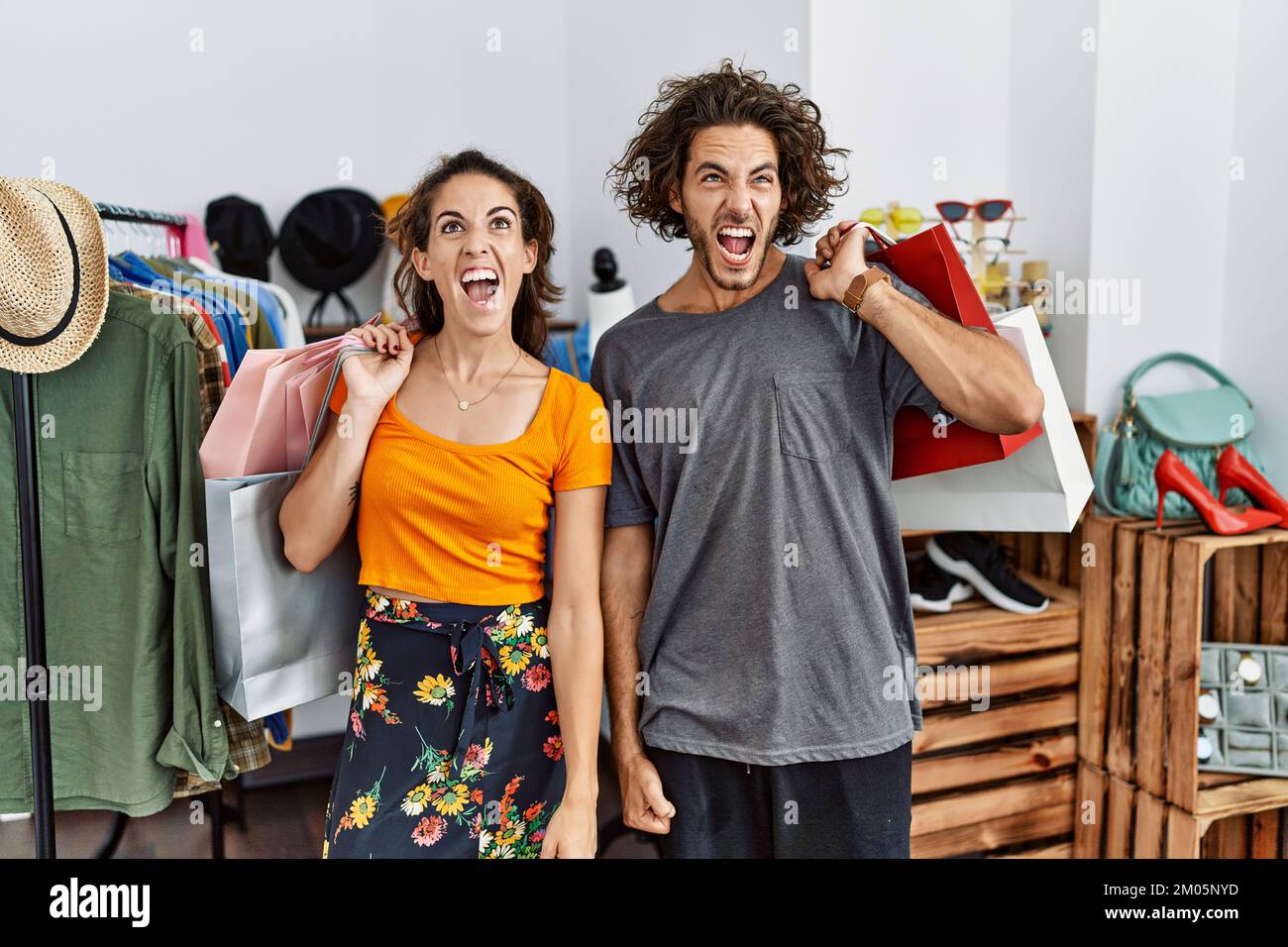 Young hispanic couple holding shopping bags at retail shop angry and ...