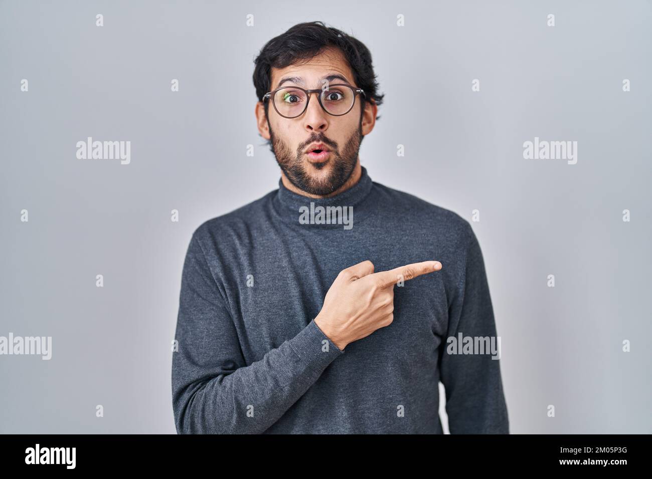 Handsome latin man standing over isolated background surprised pointing ...