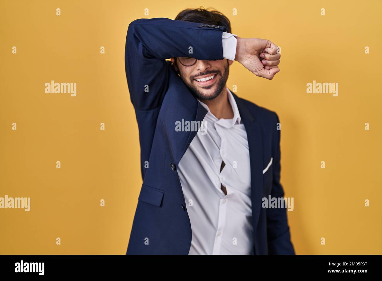 Handsome latin man standing over yellow background covering eyes with ...