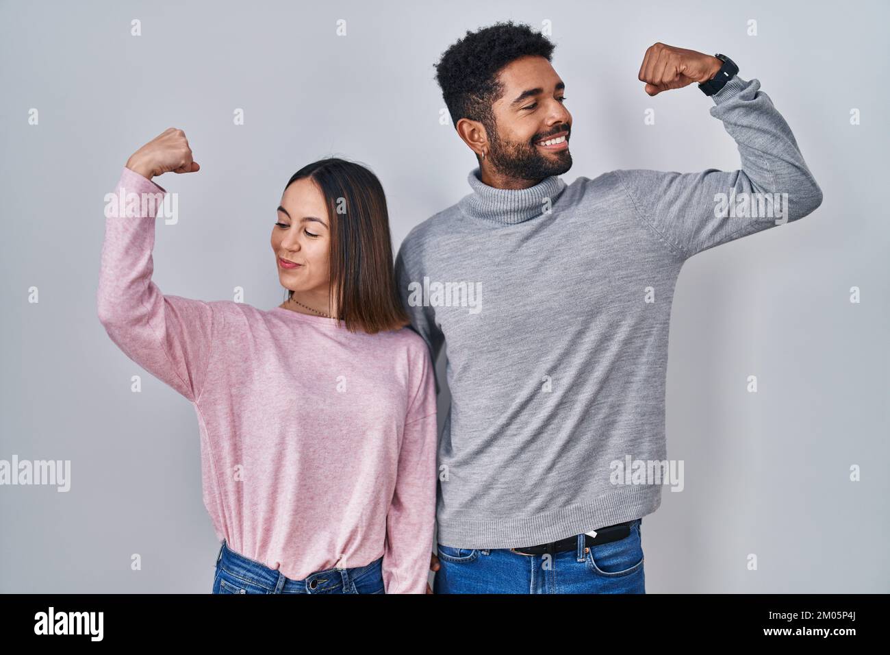 Young hispanic couple standing together showing arms muscles smiling ...