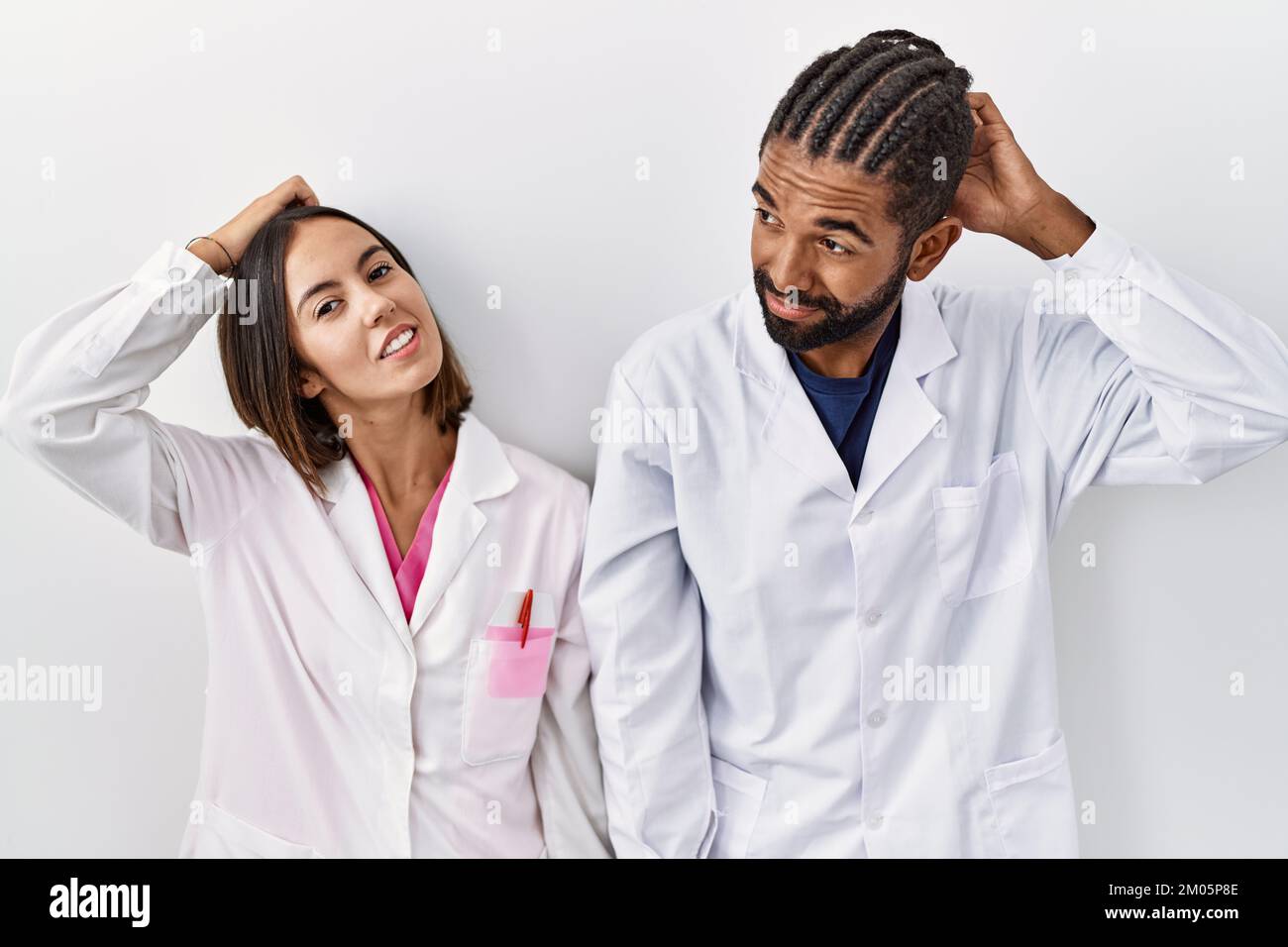 Young hispanic doctors standing over white background confuse and ...