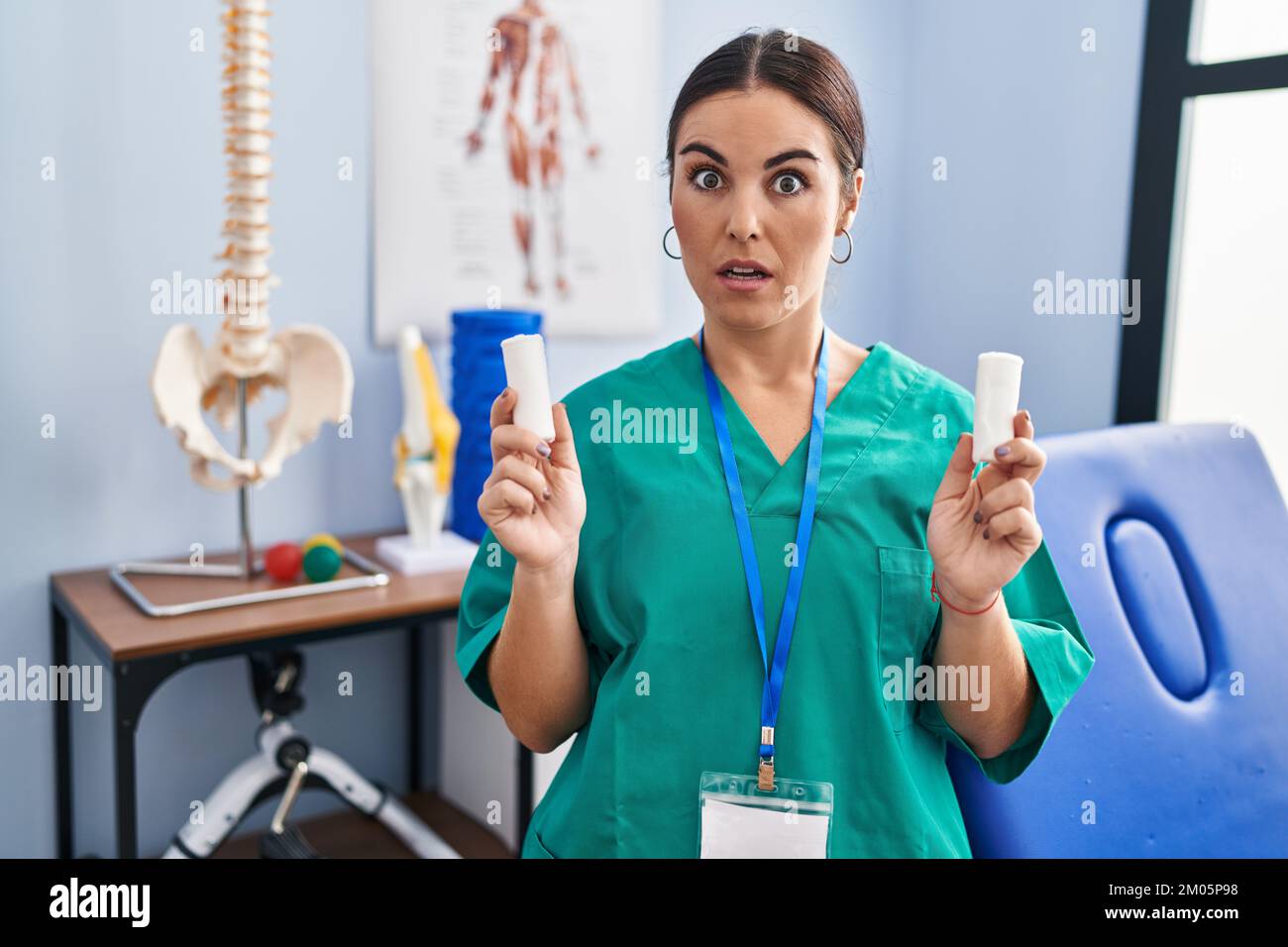 Young hispanic woman holding strip band for sprains in shock face ...