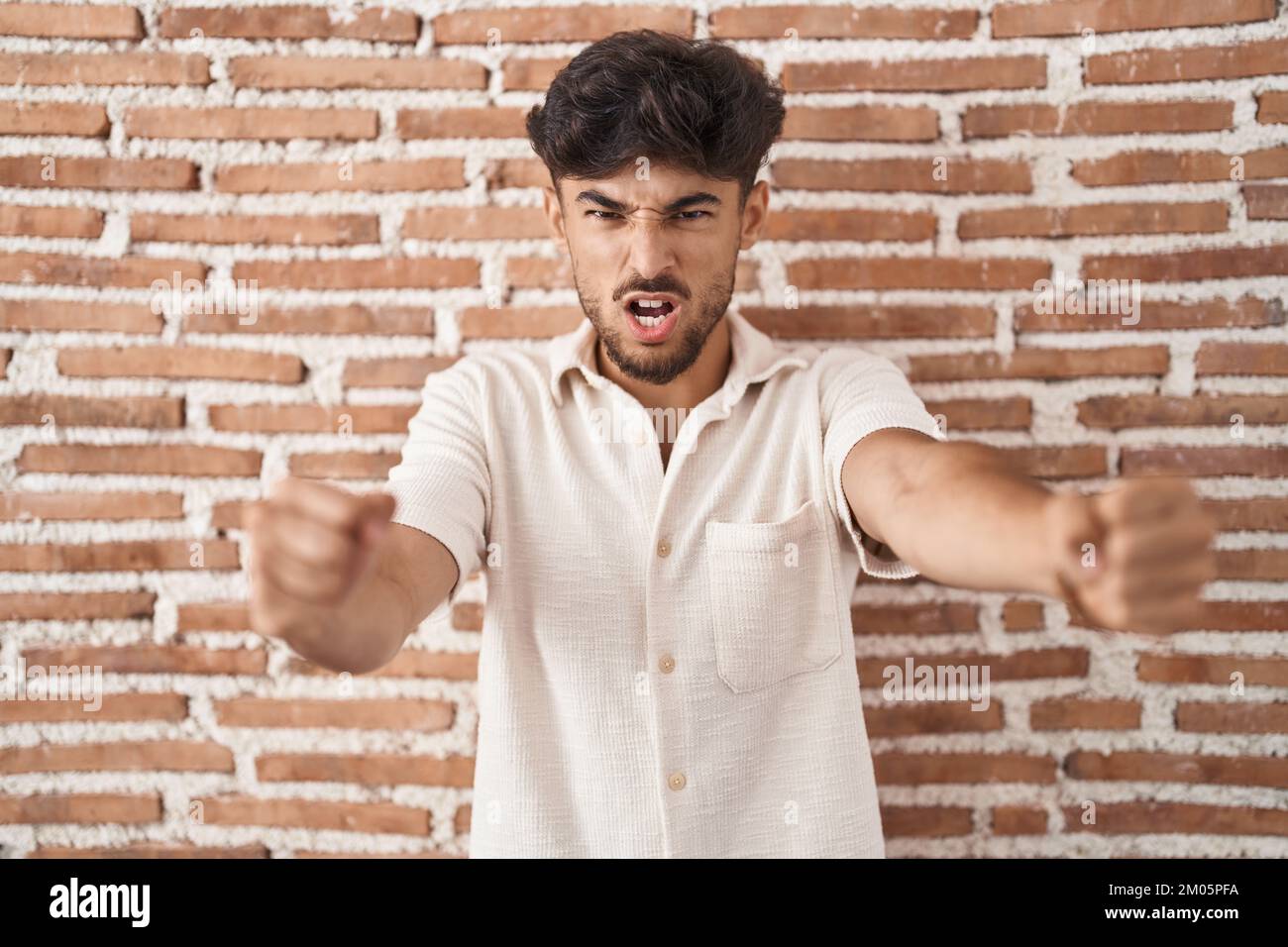 Arab man with beard standing over bricks wall background angry and mad ...