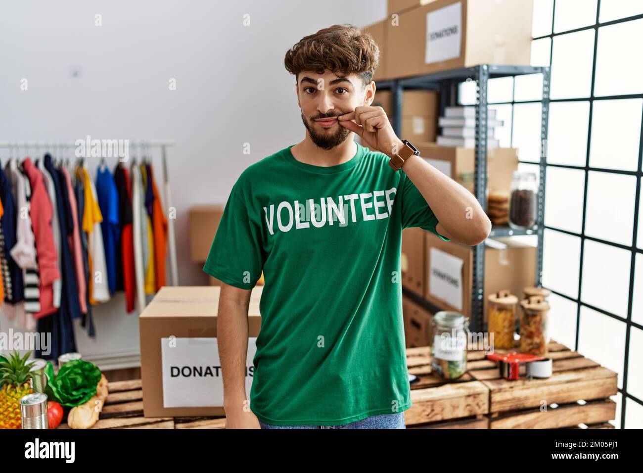Young arab man wearing volunteer t shirt at donations stand mouth and ...