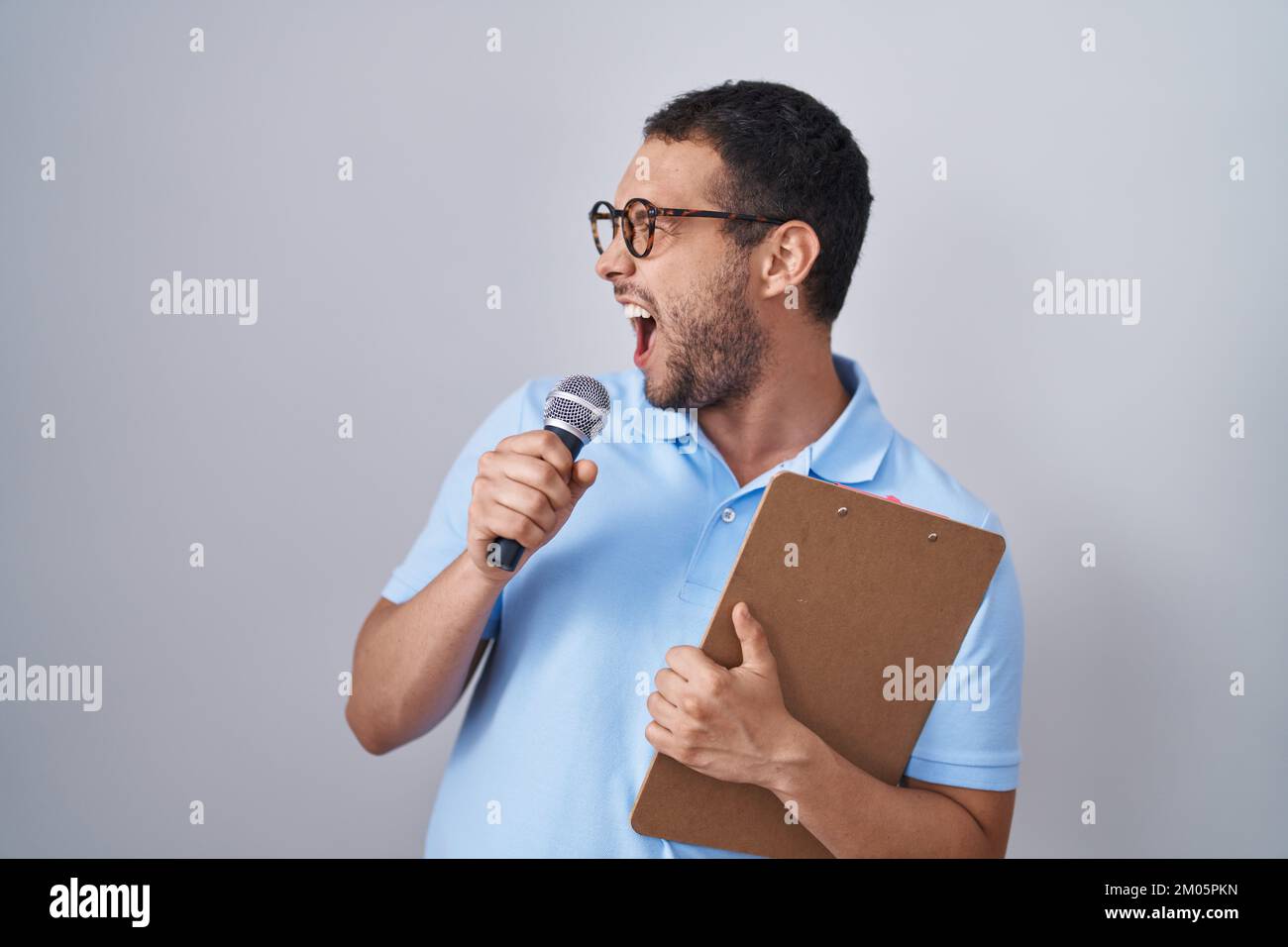 Hispanic man holding reporter microphone and clipboard angry and mad ...