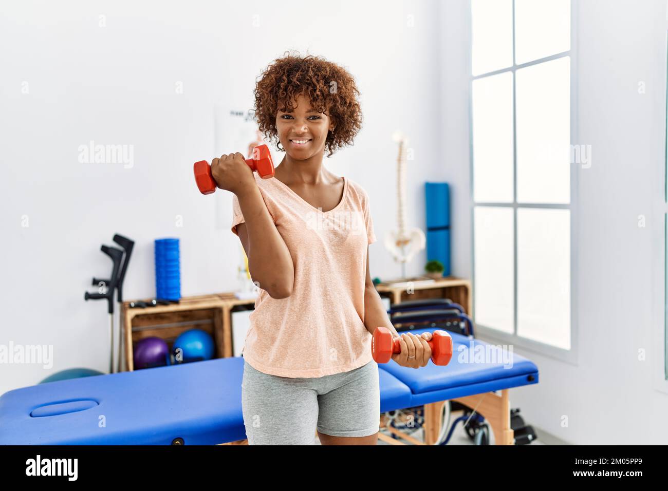 Young african american woman doing rehab using dumbbells at clinic ...