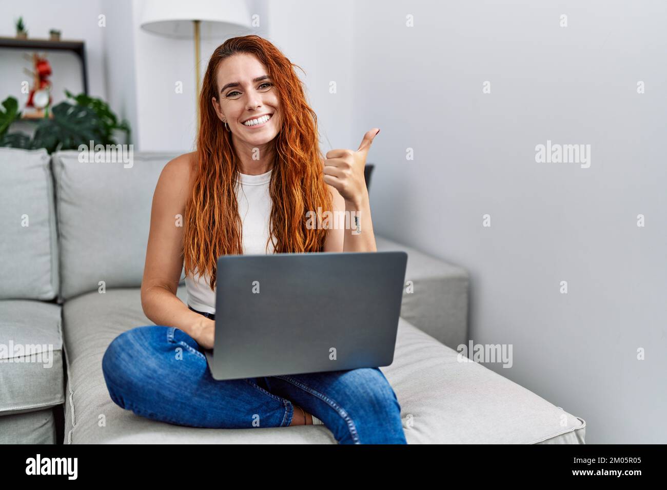 Young redhead woman using laptop at home smiling happy and positive ...