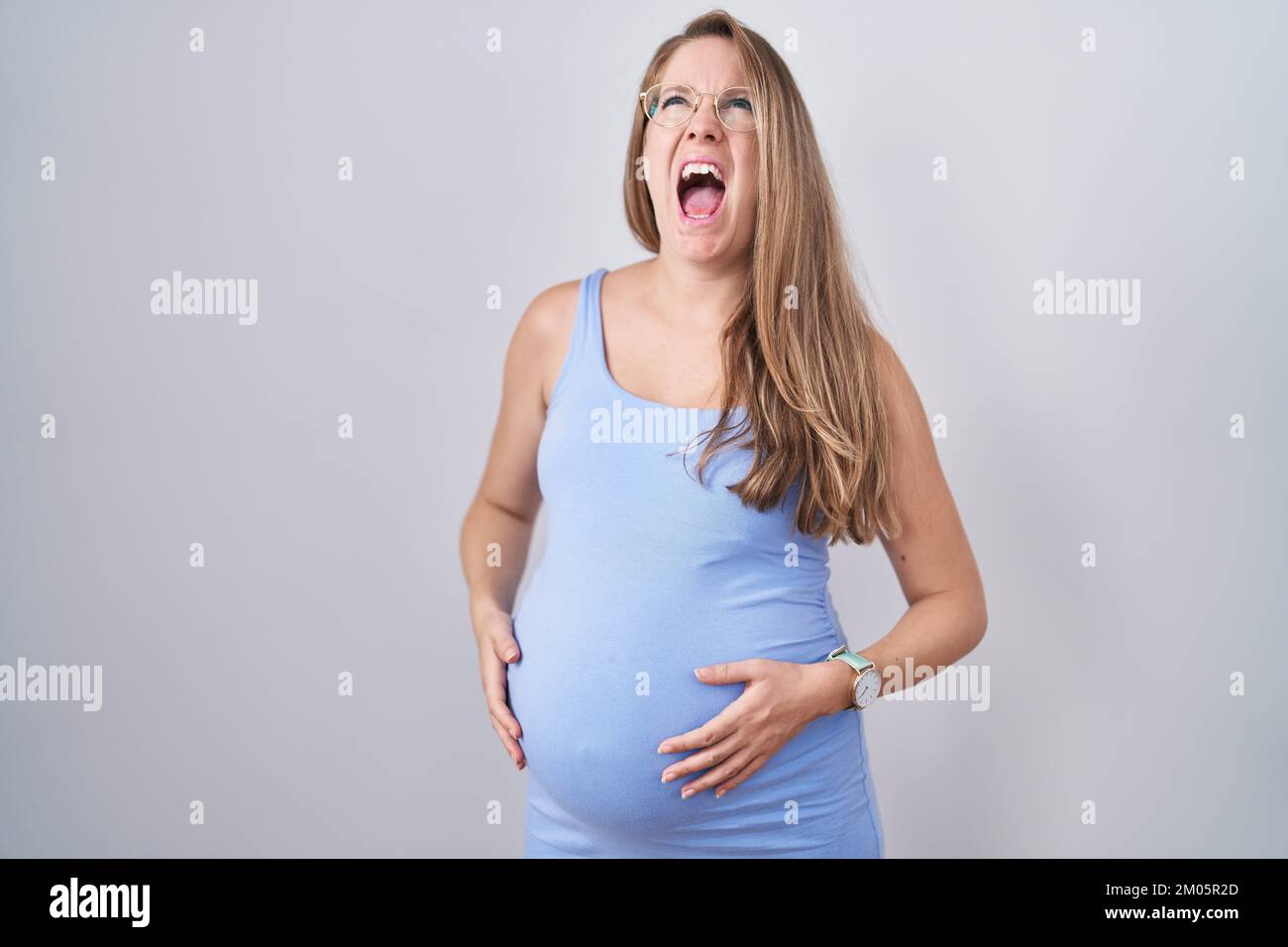 Young pregnant woman standing over white background angry and mad ...