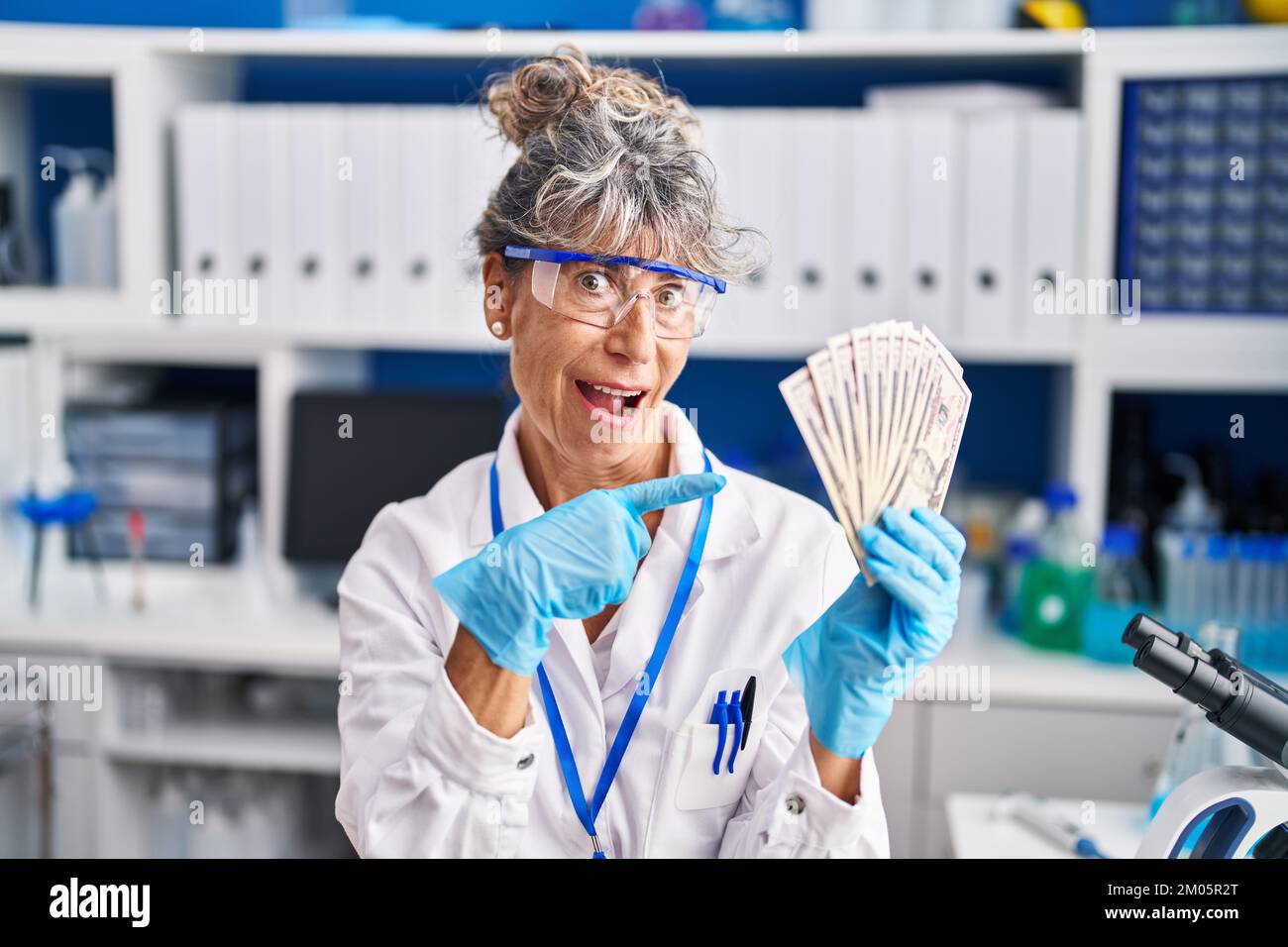Middle age woman working at scientist laboratory holding dollars ...